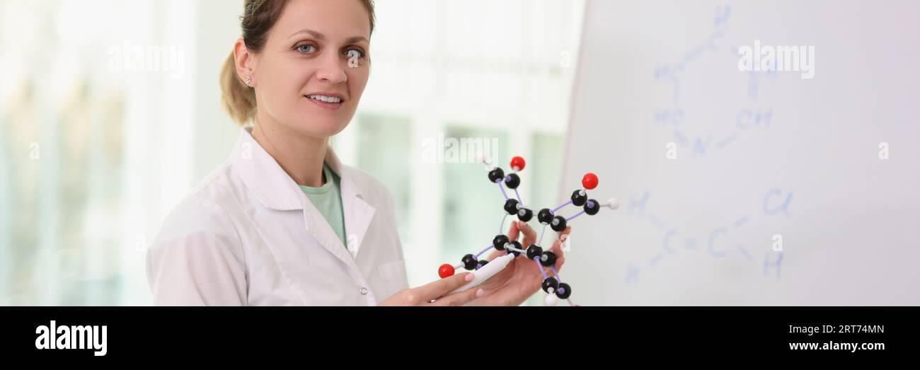 Female scientist standing near whiteboard, pointing to molecular model ...
