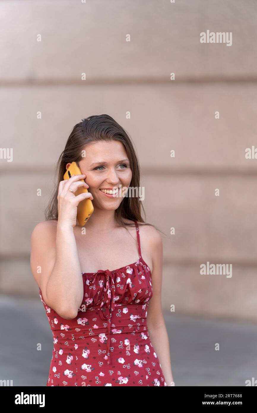 Woman in dress smiling while talking on the phone outdoors. Technology ...