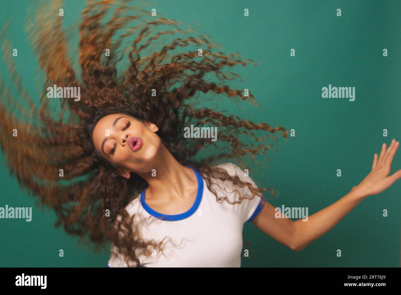 Young biracial woman dancing flipping hair, green studio background ...