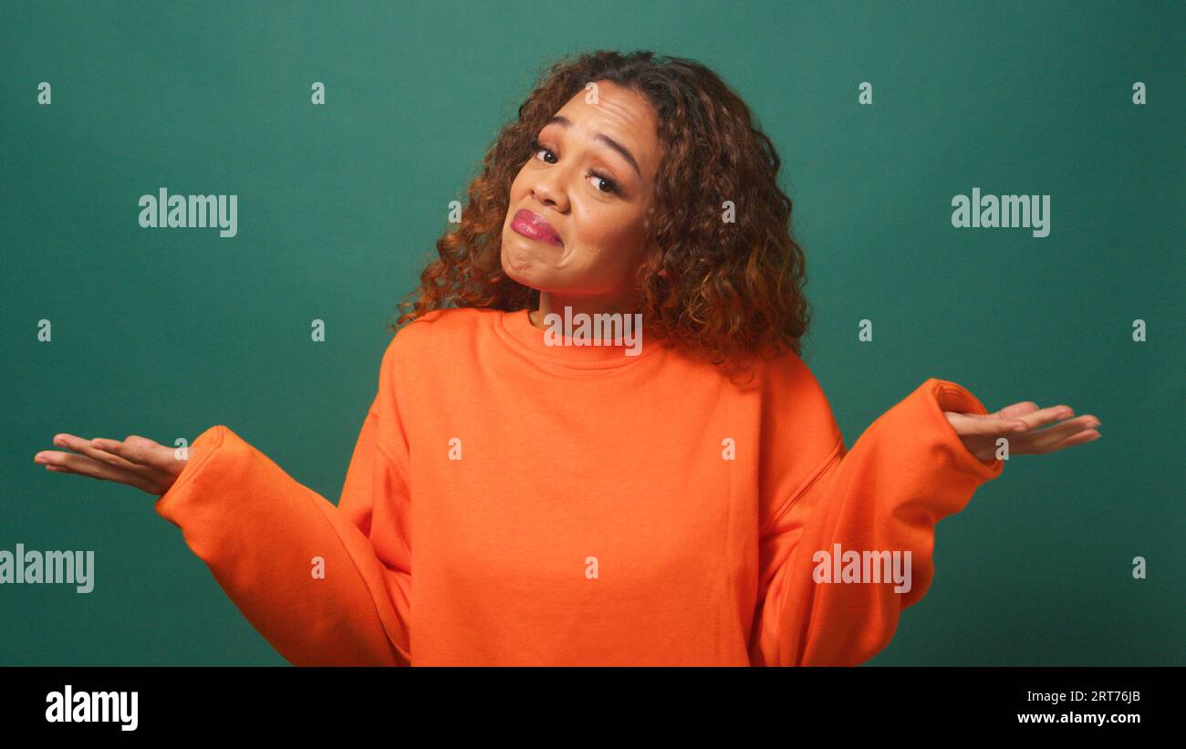 Beautiful multi-ethnic woman shrugs shoulders, green studio background ...