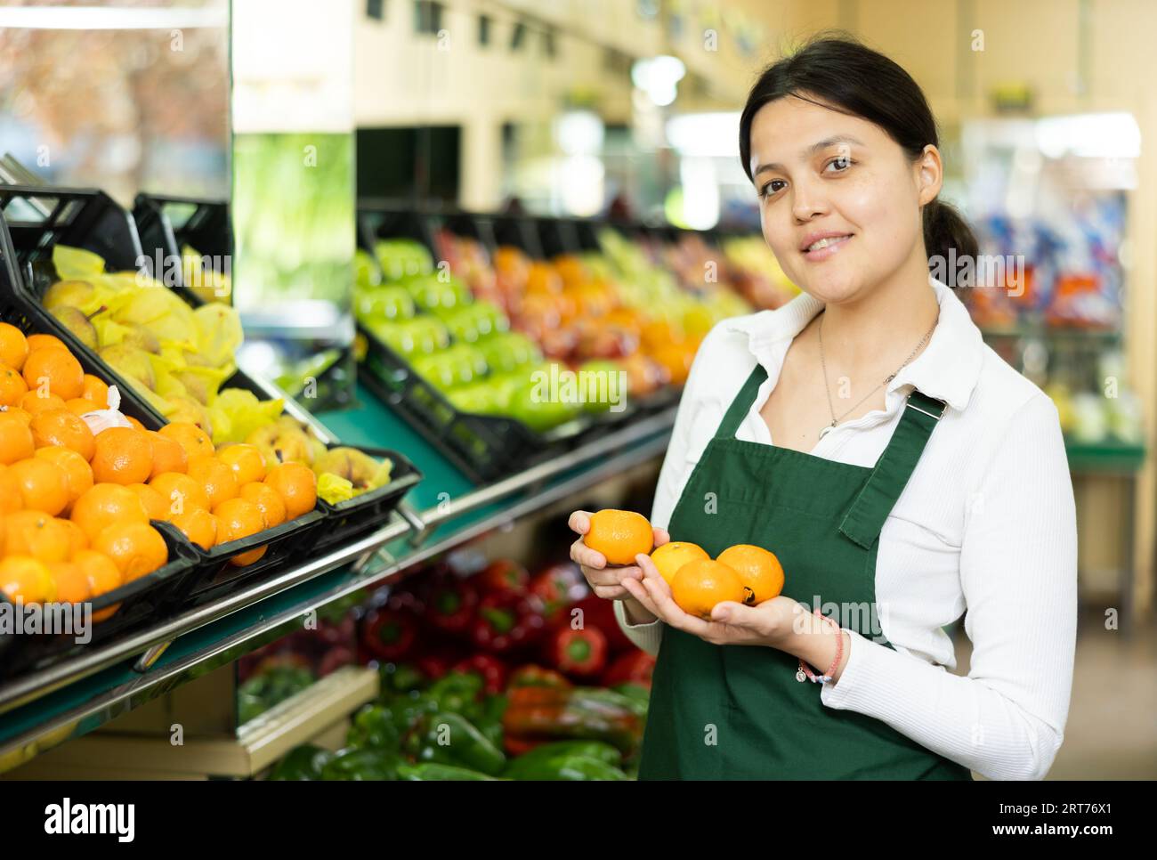 Female grocery store worker lays out ripe tangerines on counter and ...