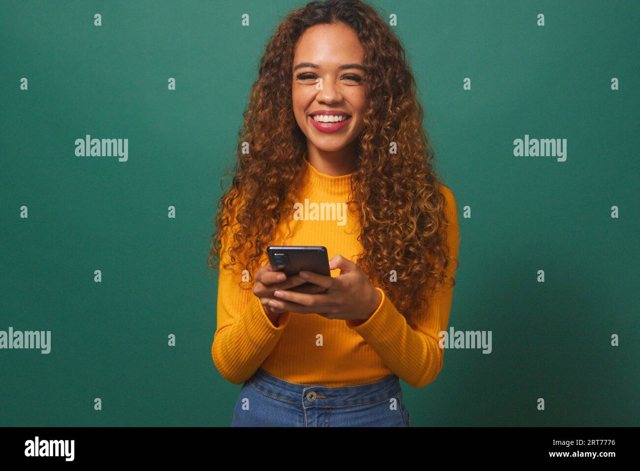 Beautiful young woman texting on cellphone, smiling, green studio ...