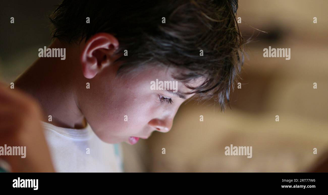 Candid young boy staring at screen at night. Child face looking at ...