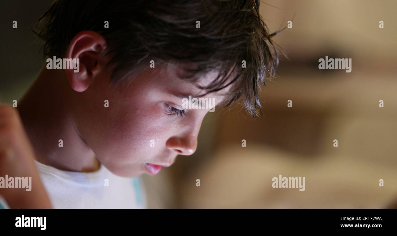 Candid young boy staring at screen at night. Child face looking at ...