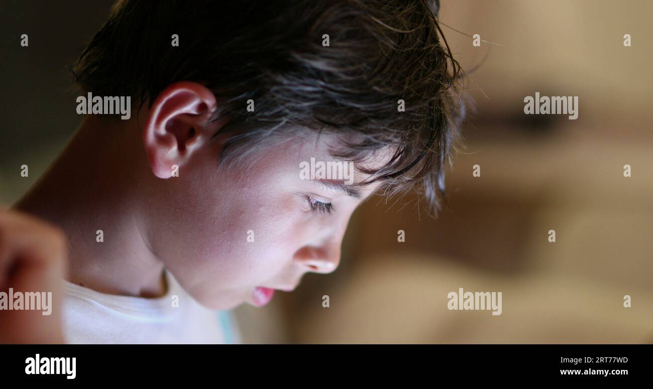 Candid young boy staring at screen at night. Child face looking at ...