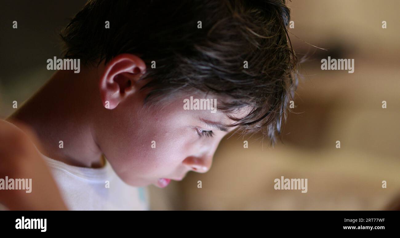 Candid young boy staring at screen at night. Child face looking at ...