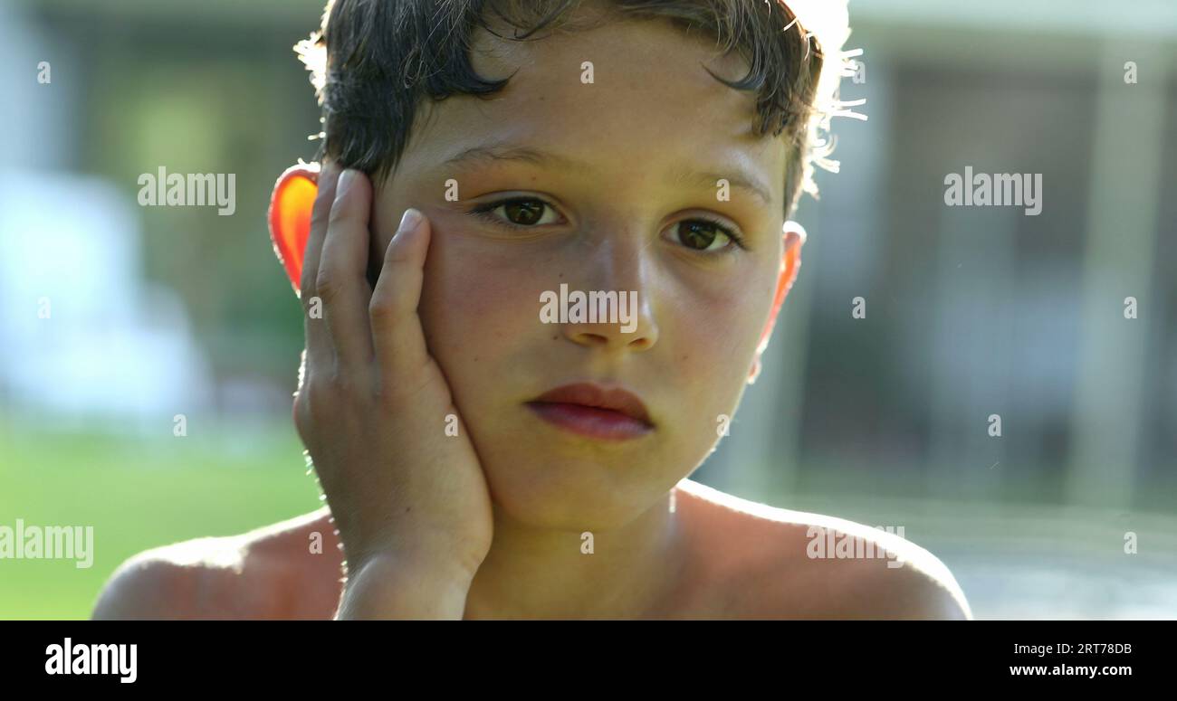 Boy scratching ear casually outside. Portrait of kid scratches body ...