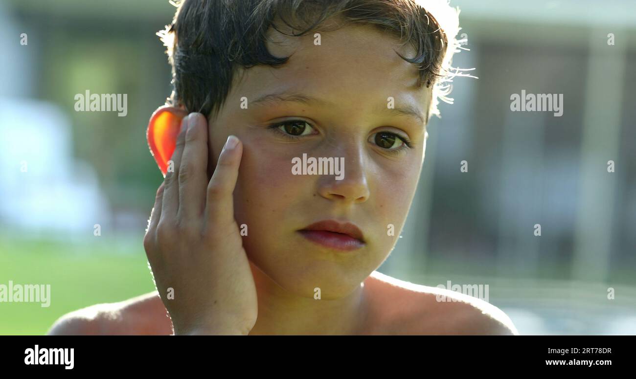 Boy scratching ear casually outside. Portrait of kid scratches body ...