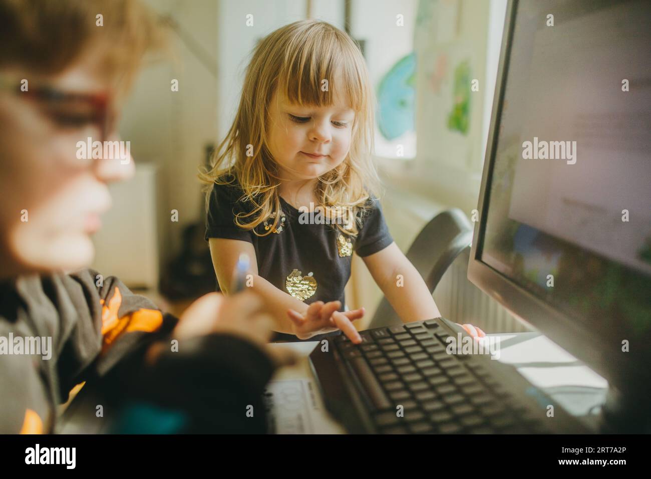 Little sister annoying her brother while he working on the computer ...