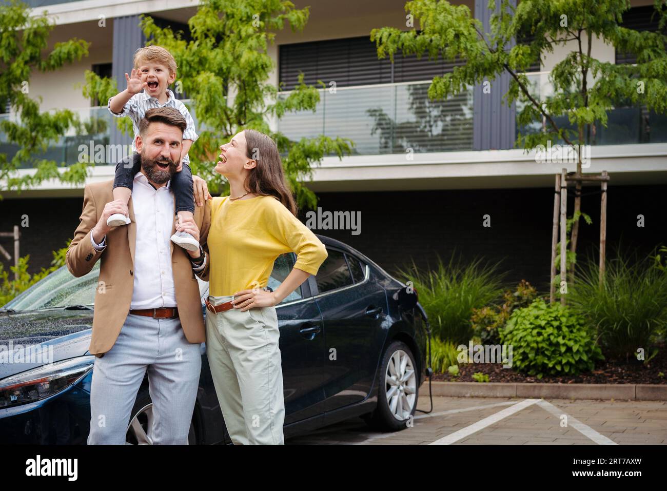 Happy family standing in front their electric car and charging it on ...