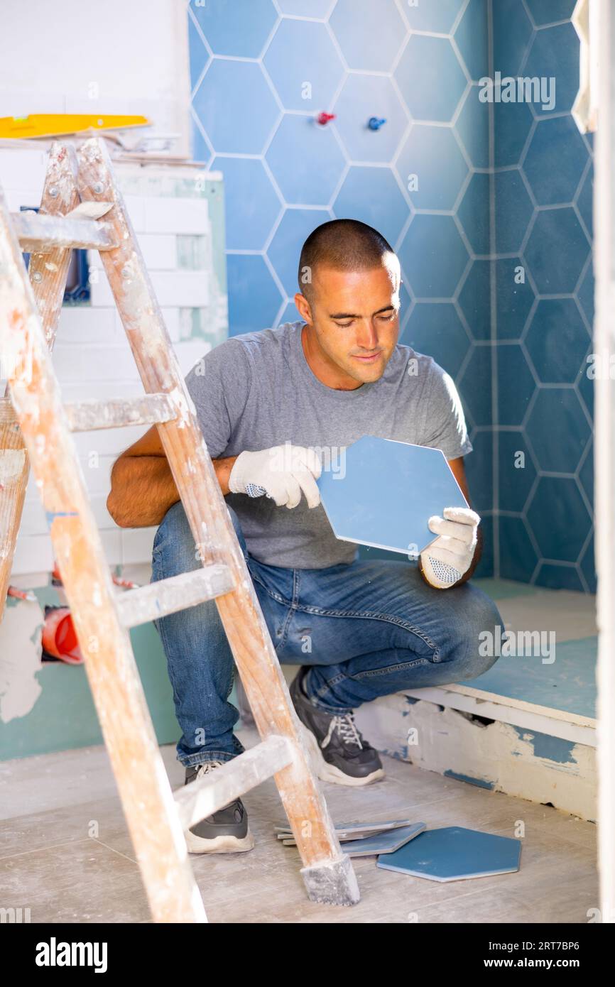 Portrait of concentrated young man sitting squat and making renovation ...
