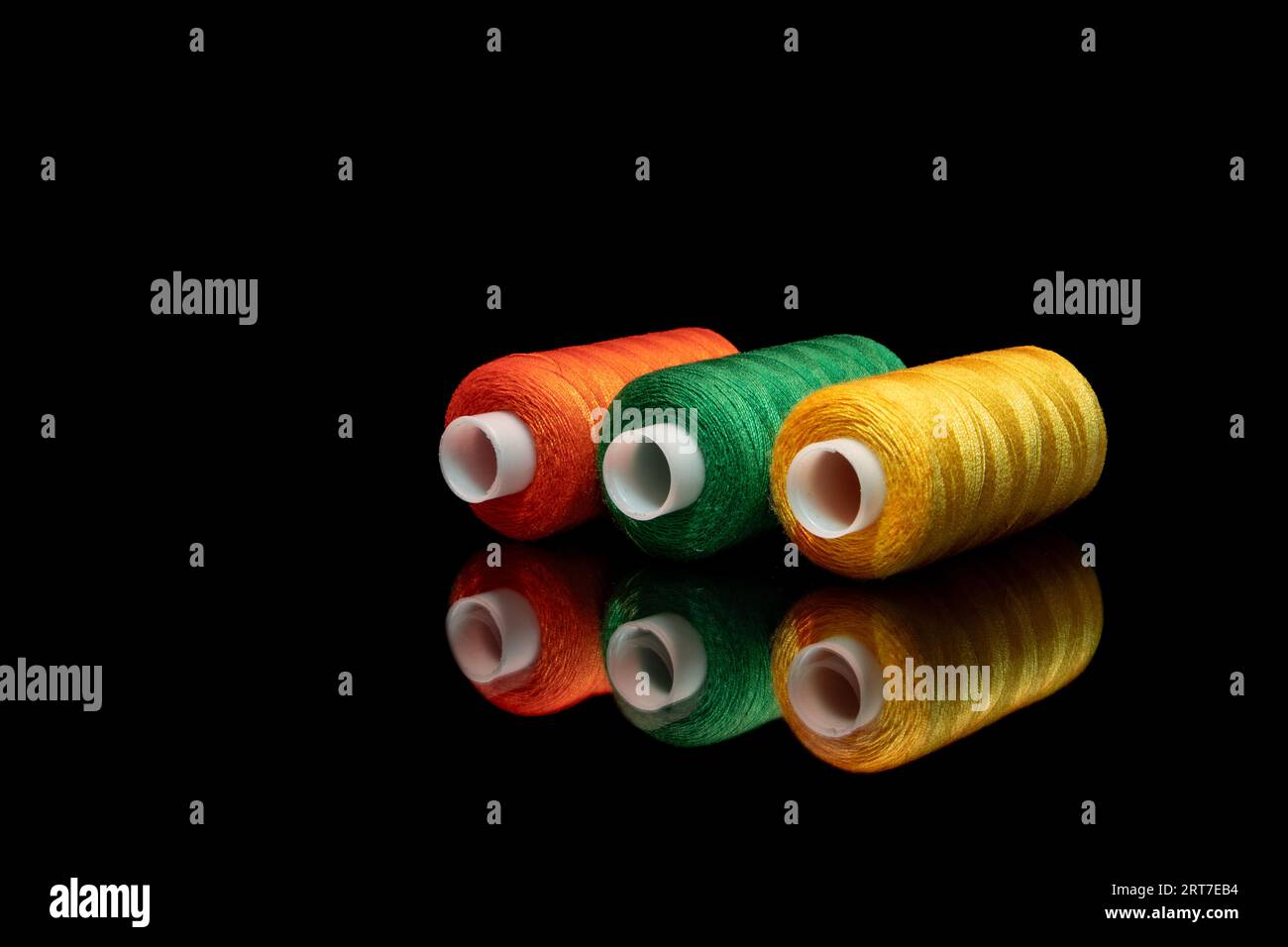 Three-color thread spools on black background with space for text, with ...