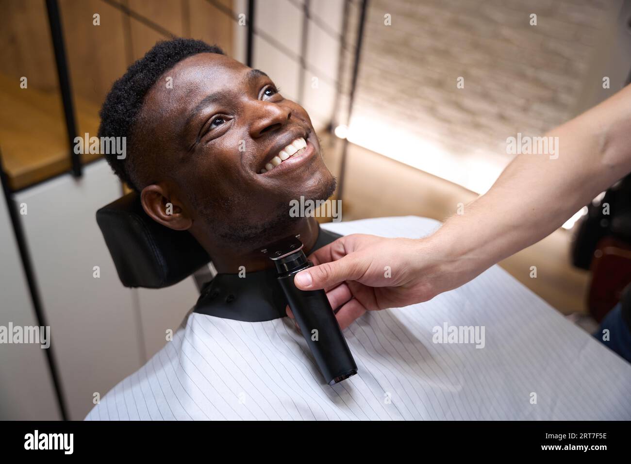 Smiling African American client sits comfortably in a barber chair ...