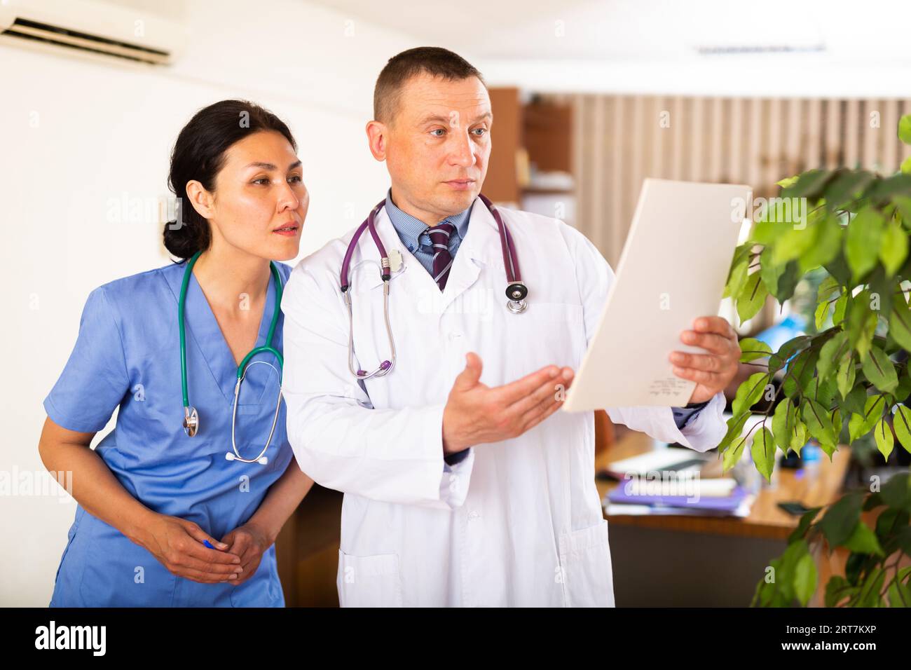 Two doctors discussing medical card of patient in office Stock Photo ...