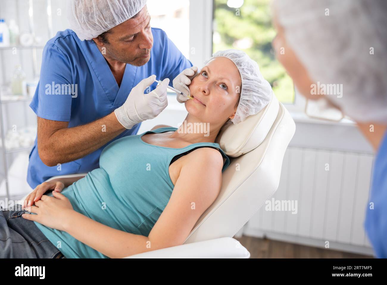 Male cosmetologist performing filler injections to correct lips contour ...