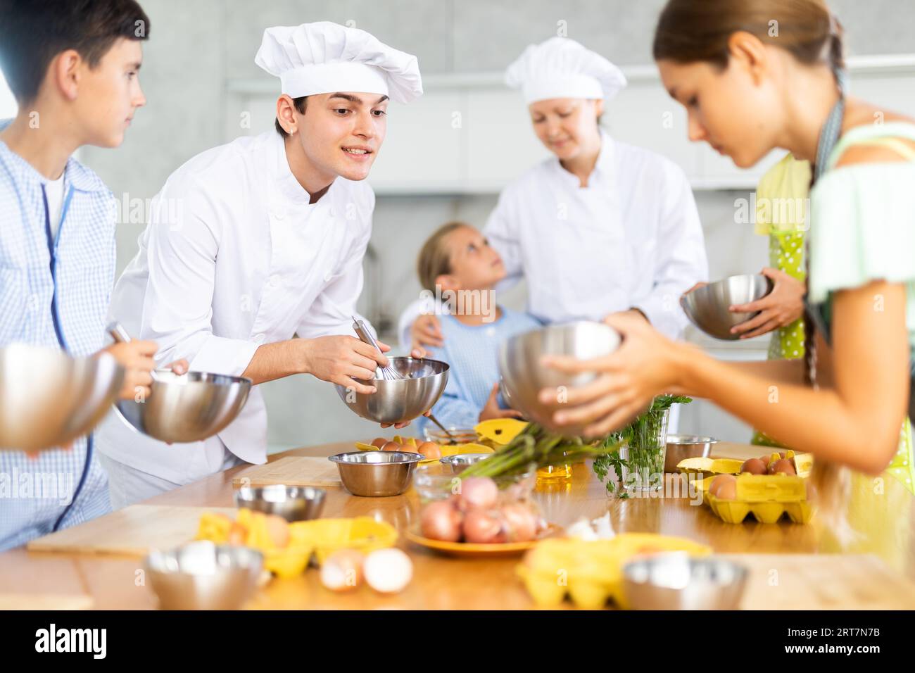 Friendly young chef running culinary courses for group of children ...