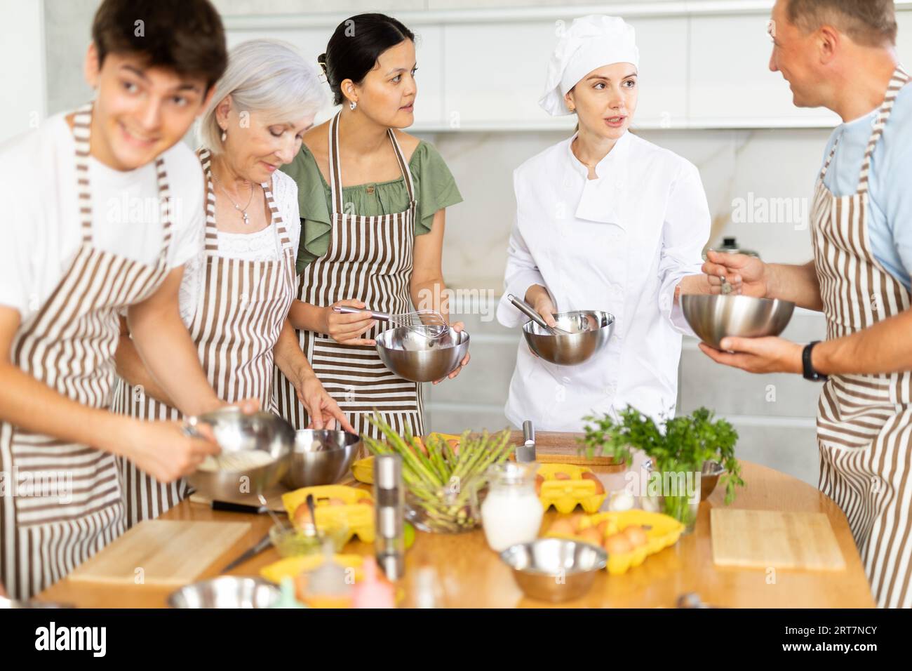 Positive young woman chef of cooking course teaching attendees how to ...