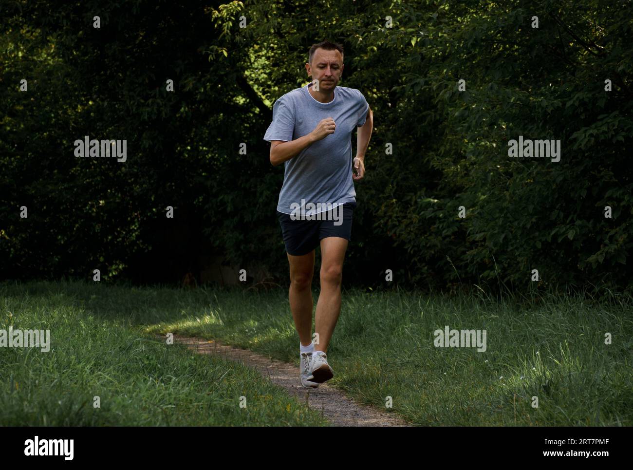 concentrated man is jogging along the path in the park in summer ...