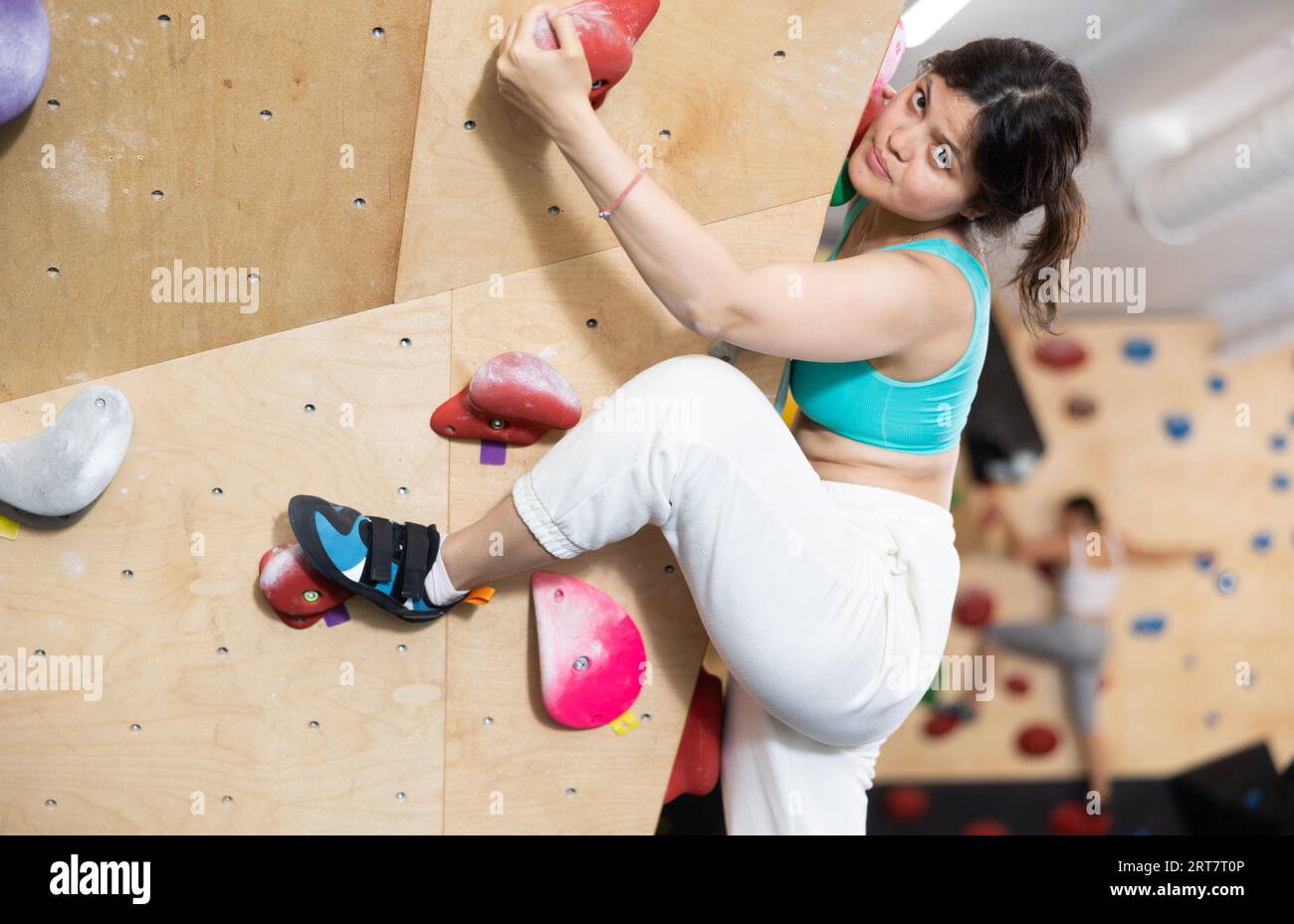 Sporty woman climbing on bouldering wall demonstrating physical strength, technical skill, and ...