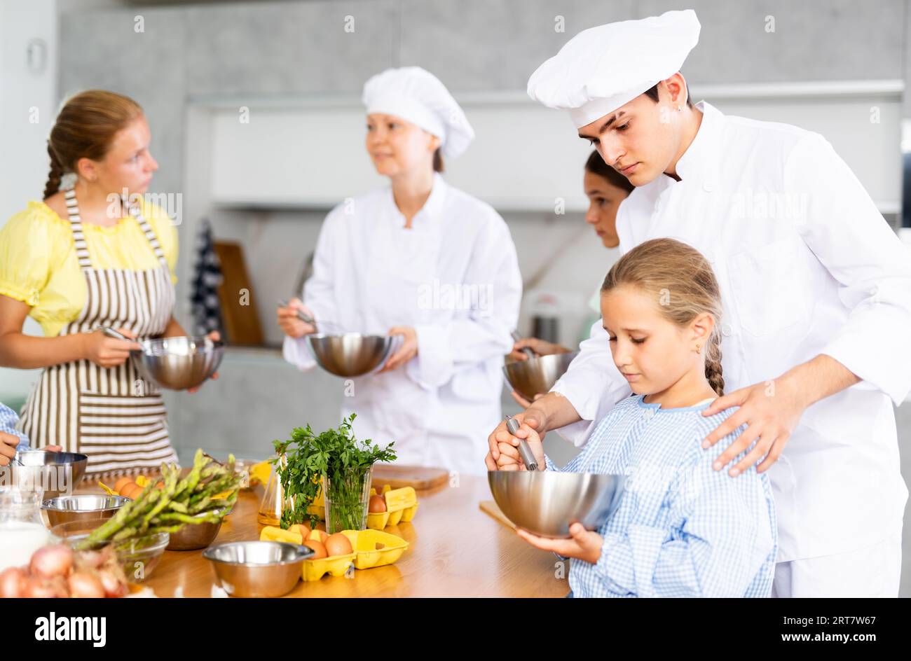 While children cooking class, male chef help small girl thoroughly stir ...