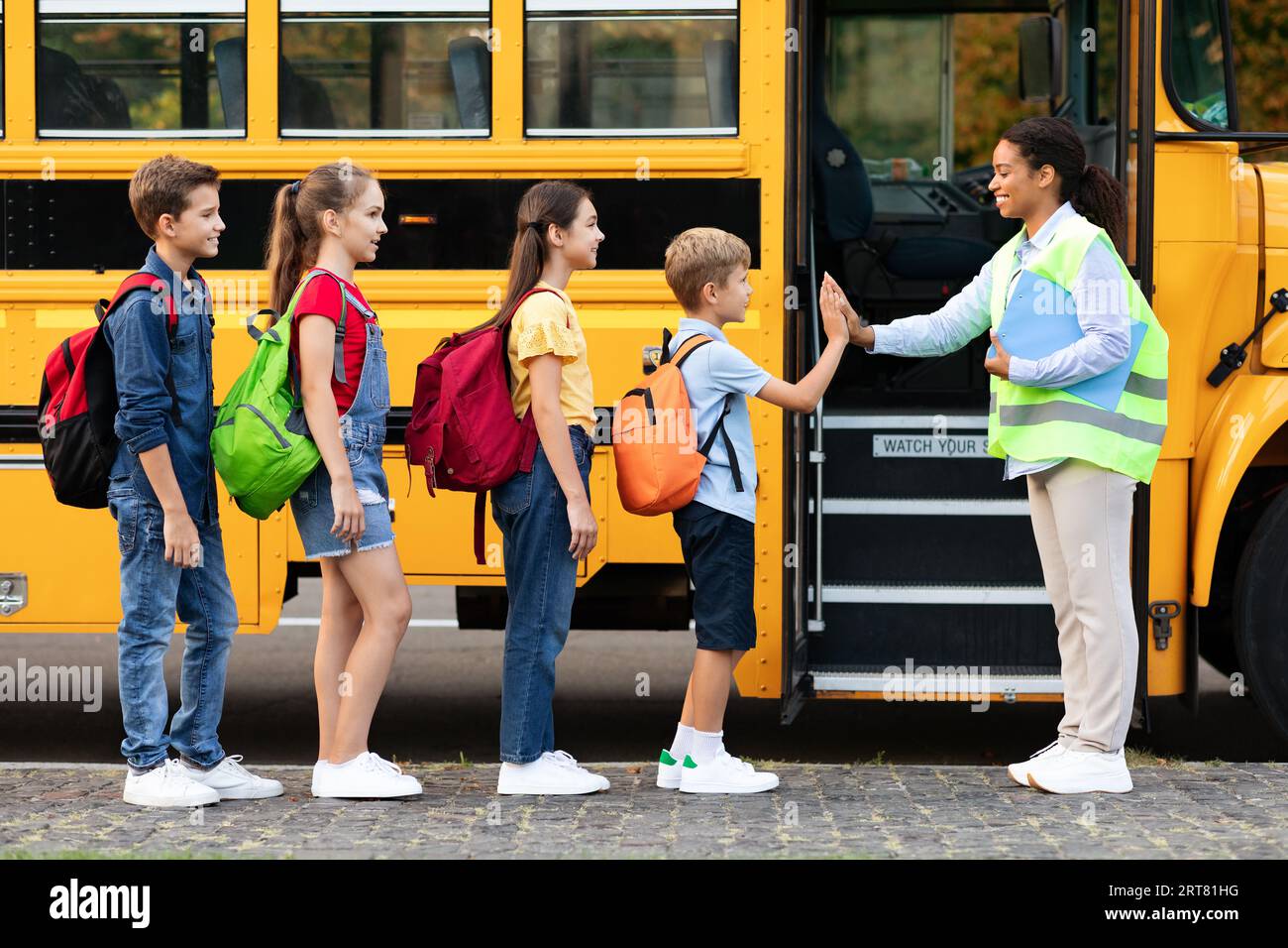 Teacher in uniform giving high five to kids entering school bus Stock ...