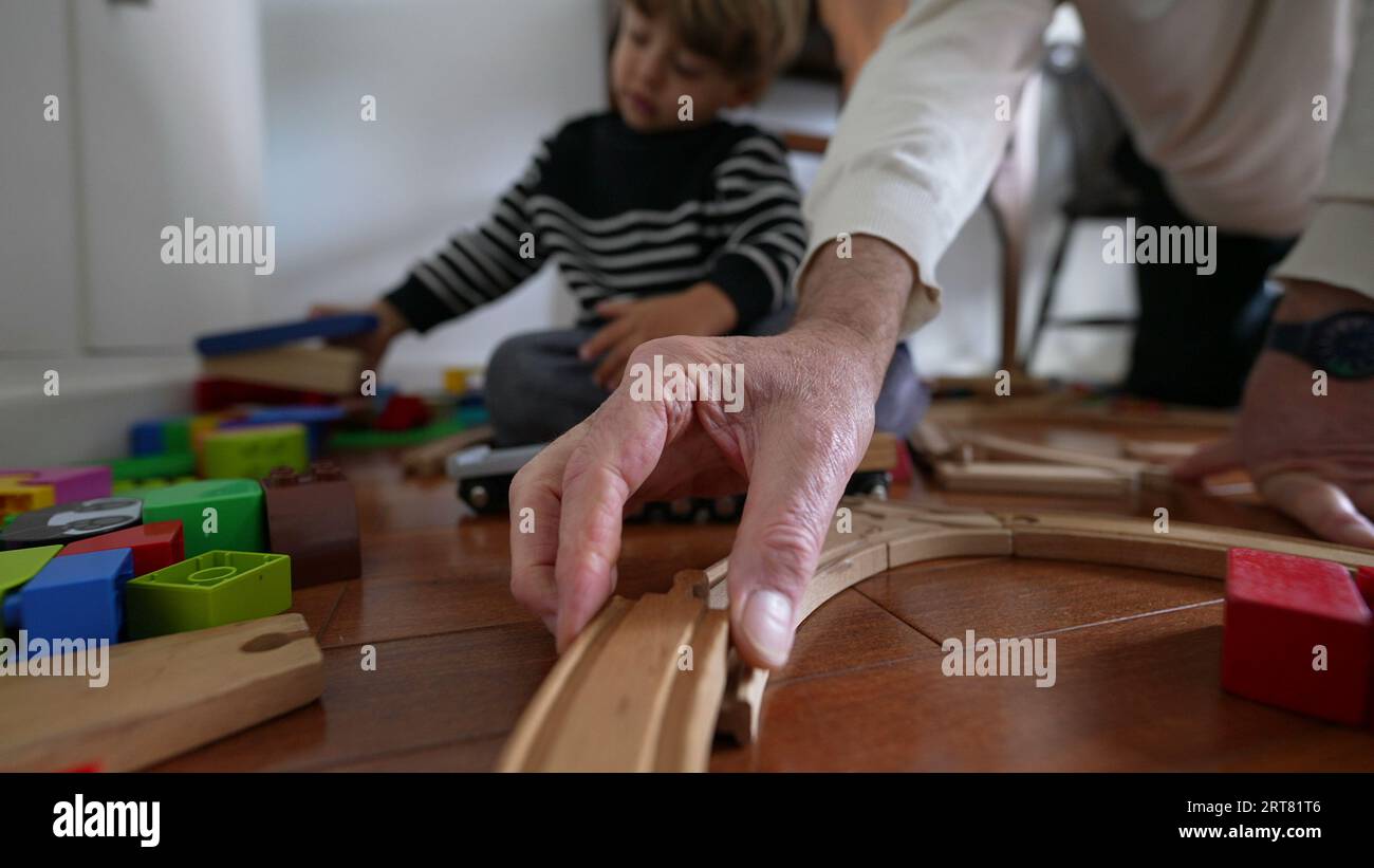 Grandfather putting train piece into wooden track, bonding family ...