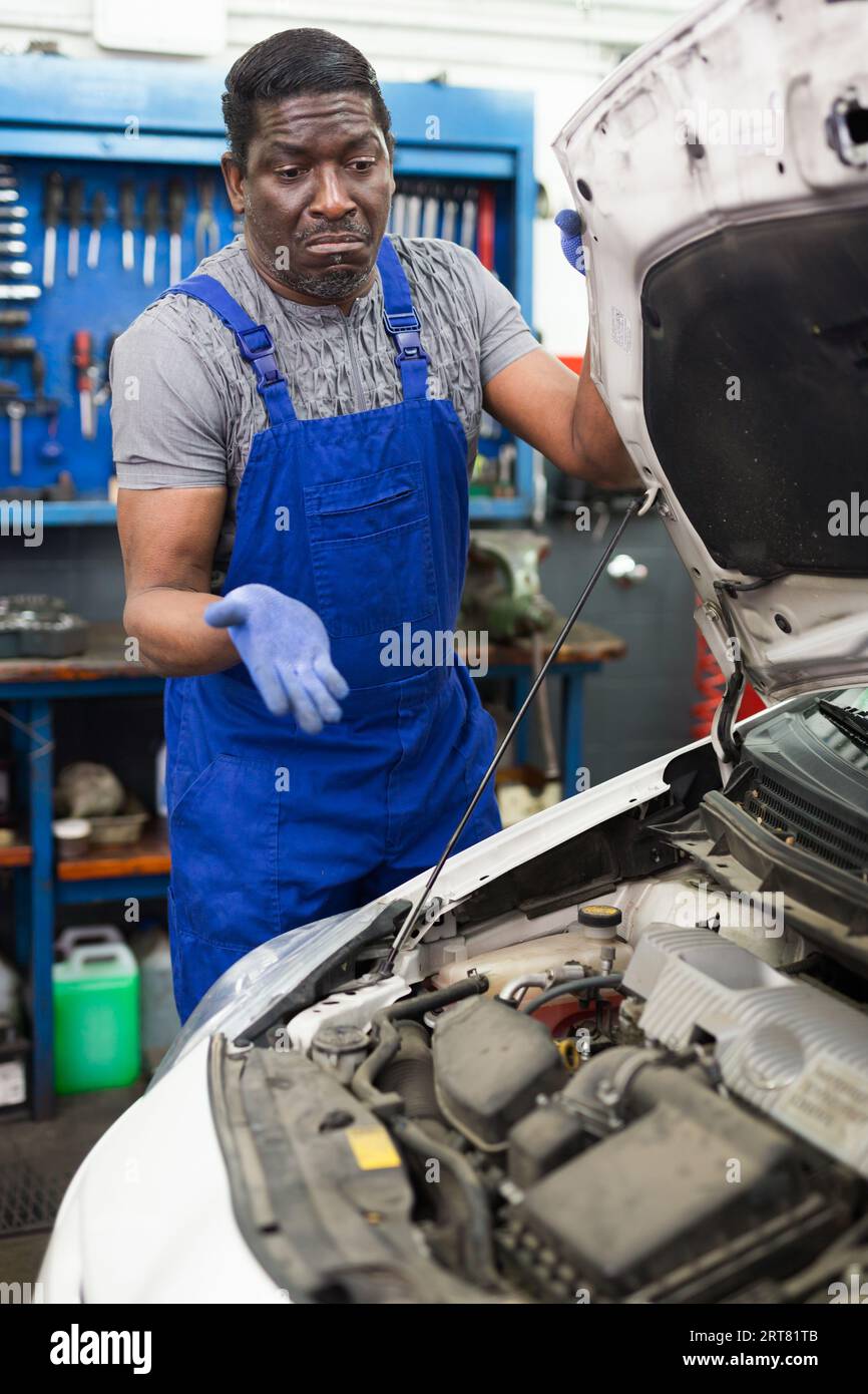 Professional american mechanic man in uniform repairing car engine ...