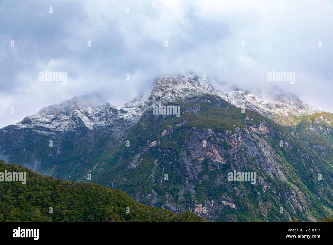 Photograph of cloud covered snow capped mountains with lush foliage in ...