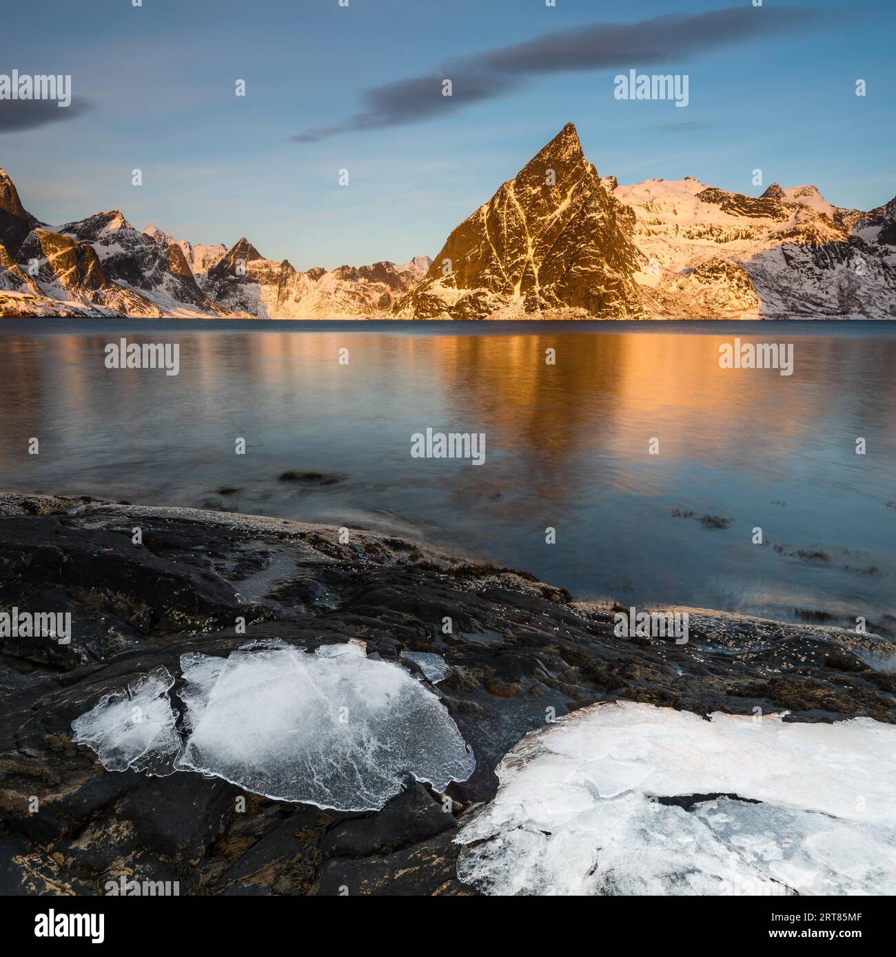 Ice sheets on dark rock with lake and snow-clad steep mountains in the ...