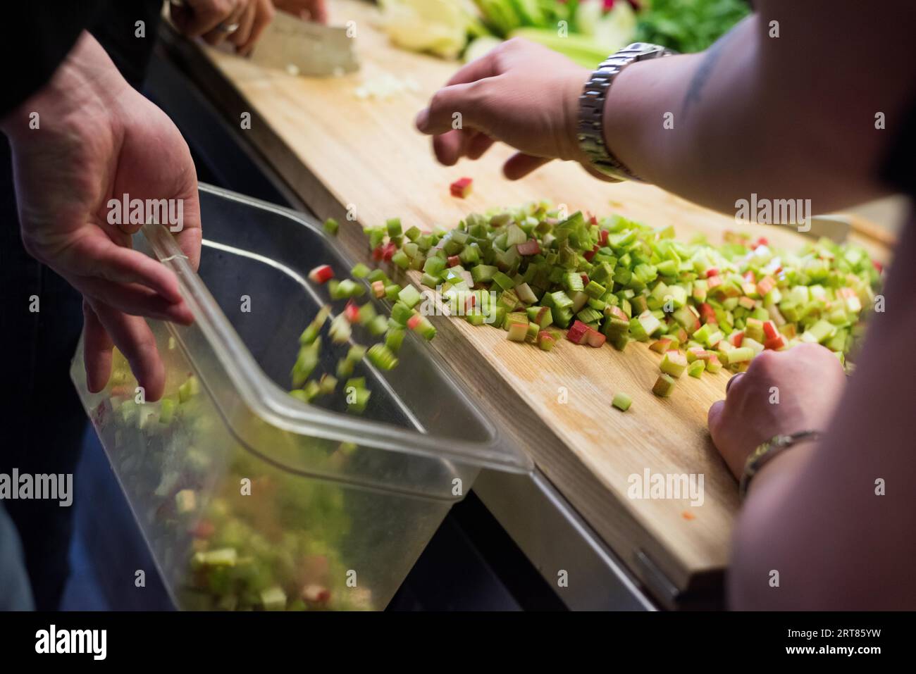 Human hands scooping cubes of cut rhubarb from wooden cutting board ...