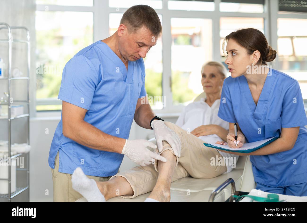 Male doctor and assistant study health status of elderly woman patient ...