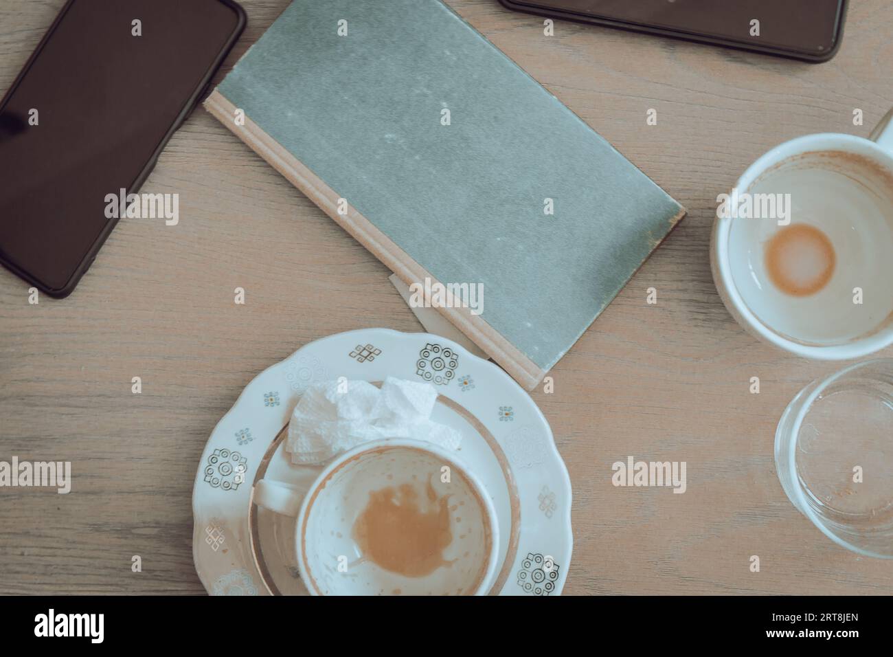 Two empty coffee cups, book and mobile phones on wooden table ...