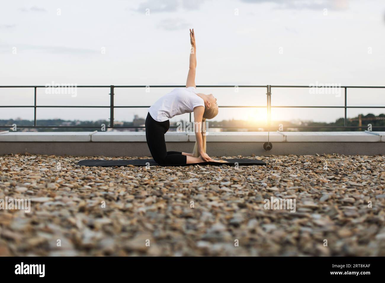Lady exercising back-bend pose while kneeling on gravel roof Stock ...