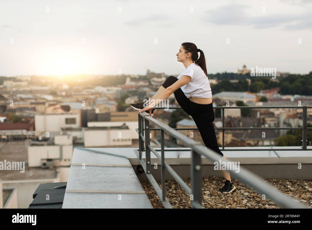 Woman putting leg on handrail after training on rooftop Stock Photo - Alamy