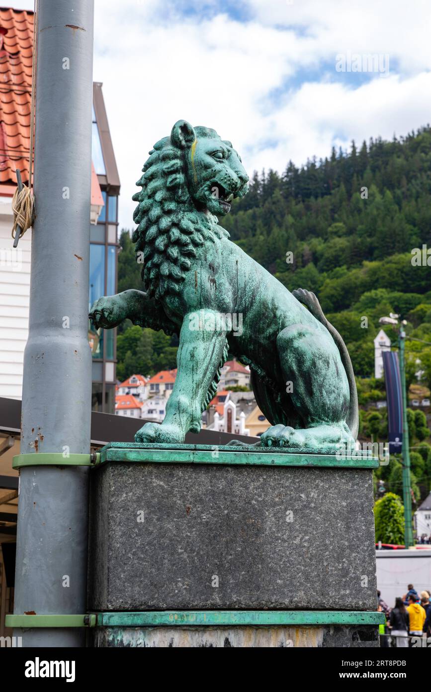 Lion statue at Bryggen. Tourists explore the UNESCO World Heritage site ...