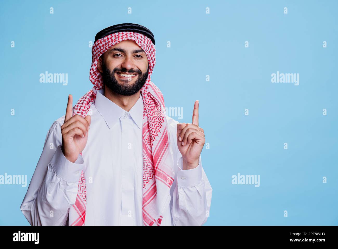 Smiling muslim man wearing traditional culture clothes and pointing up ...