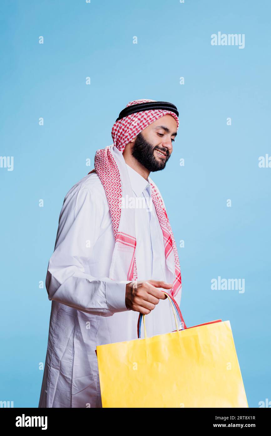 Happy consumer dressed in traditional muslim clothes carrying yellow ...