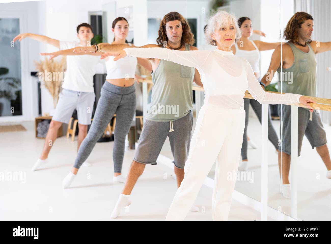 Aged woman choreographer demonstrates ballet stances to students in a ...