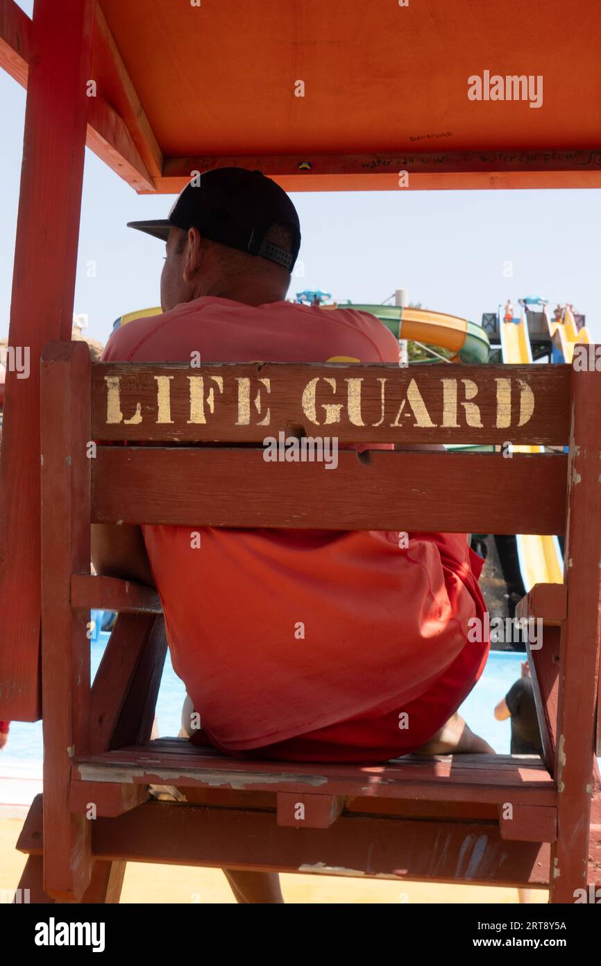 Lifeguard in a tower watching people at a swimming pool or water park ...