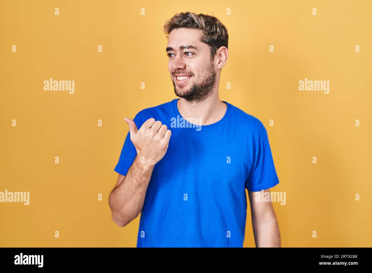Hispanic man with beard standing over yellow background smiling with ...