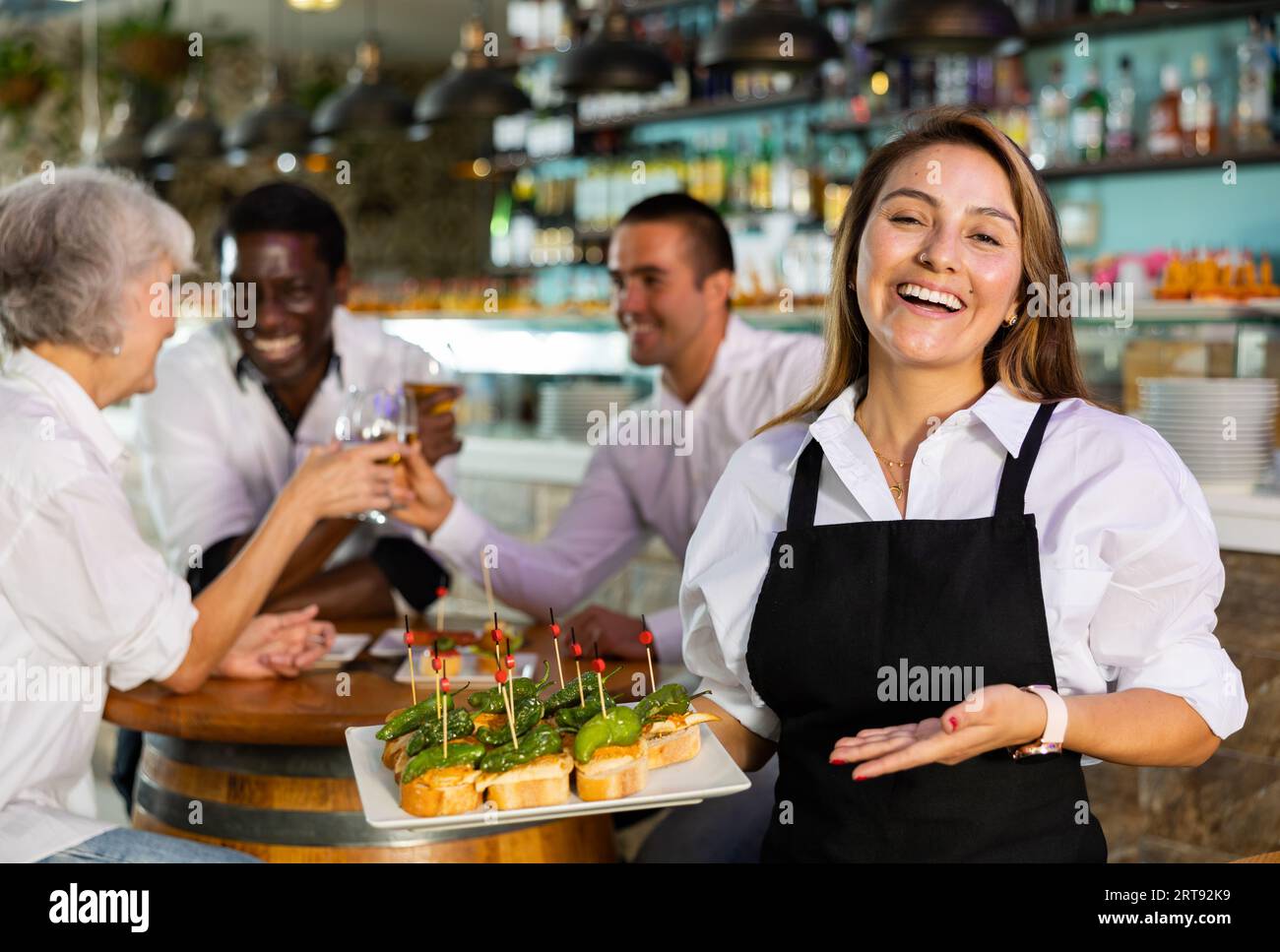 Happy Latin female waiter in uniform pointing hand on the plate with ...