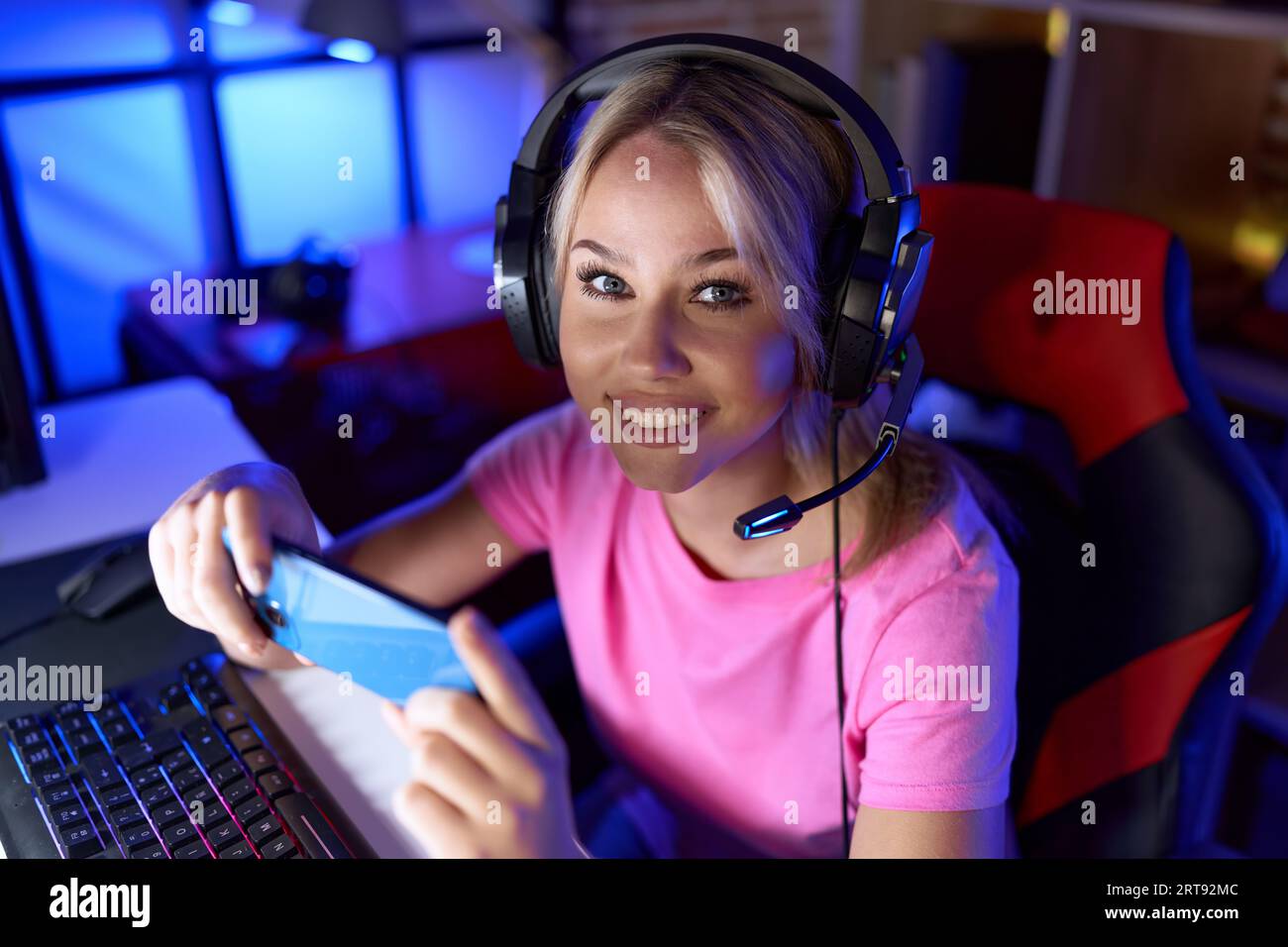 Young blonde woman streamer playing video game using smartphone at ...