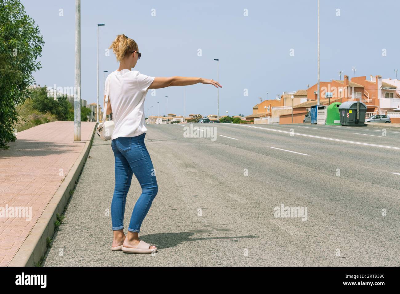 beautiful girl in t-shirt and jeans stands on the road with her back to ...