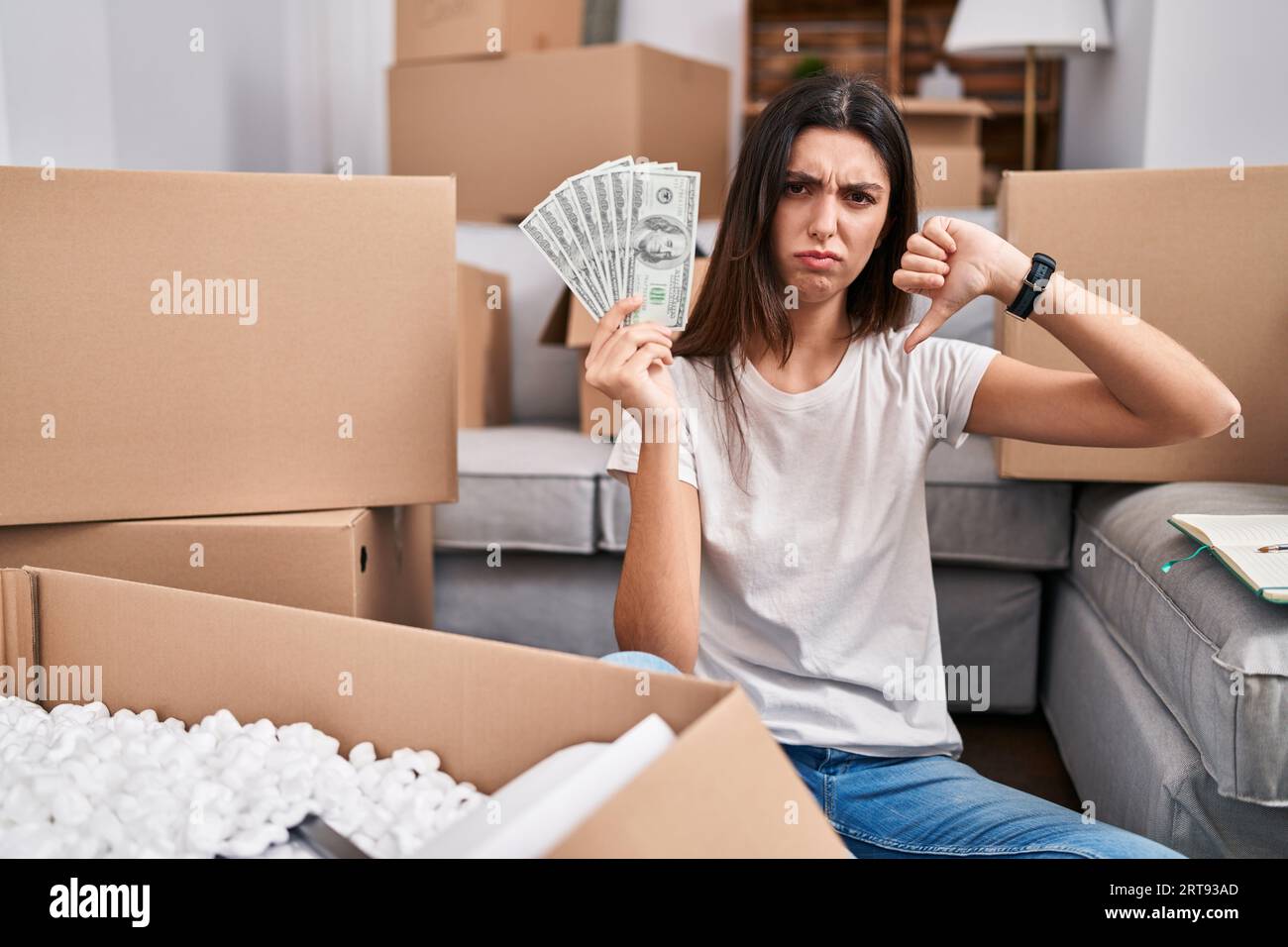 Young beautiful woman sitting on the floor at new home holding money ...