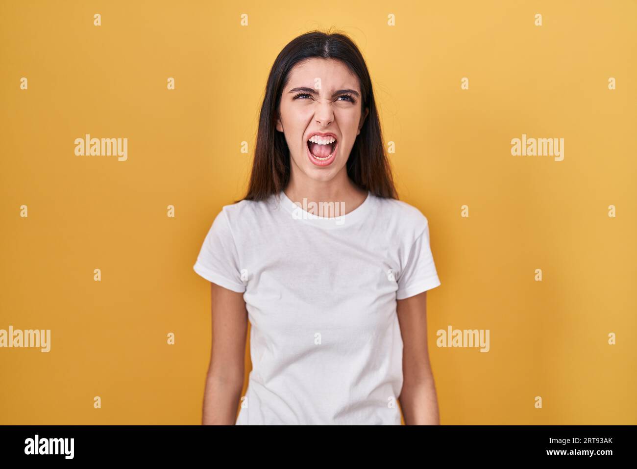 Young beautiful woman standing over yellow background angry and mad ...