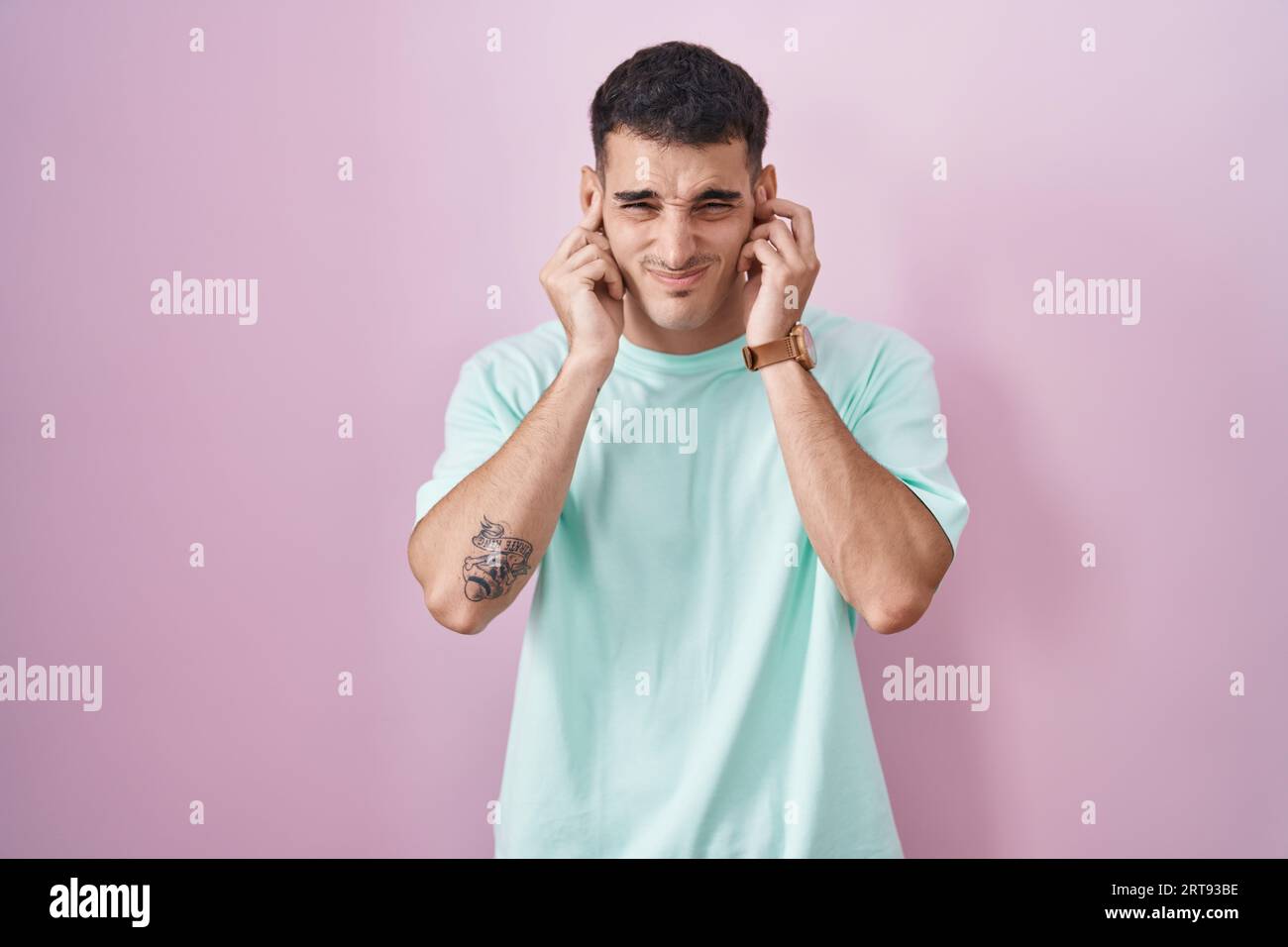 Handsome hispanic man standing over pink background covering ears with ...