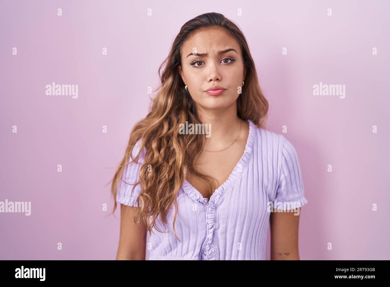 Young hispanic woman standing over pink background skeptic and nervous ...