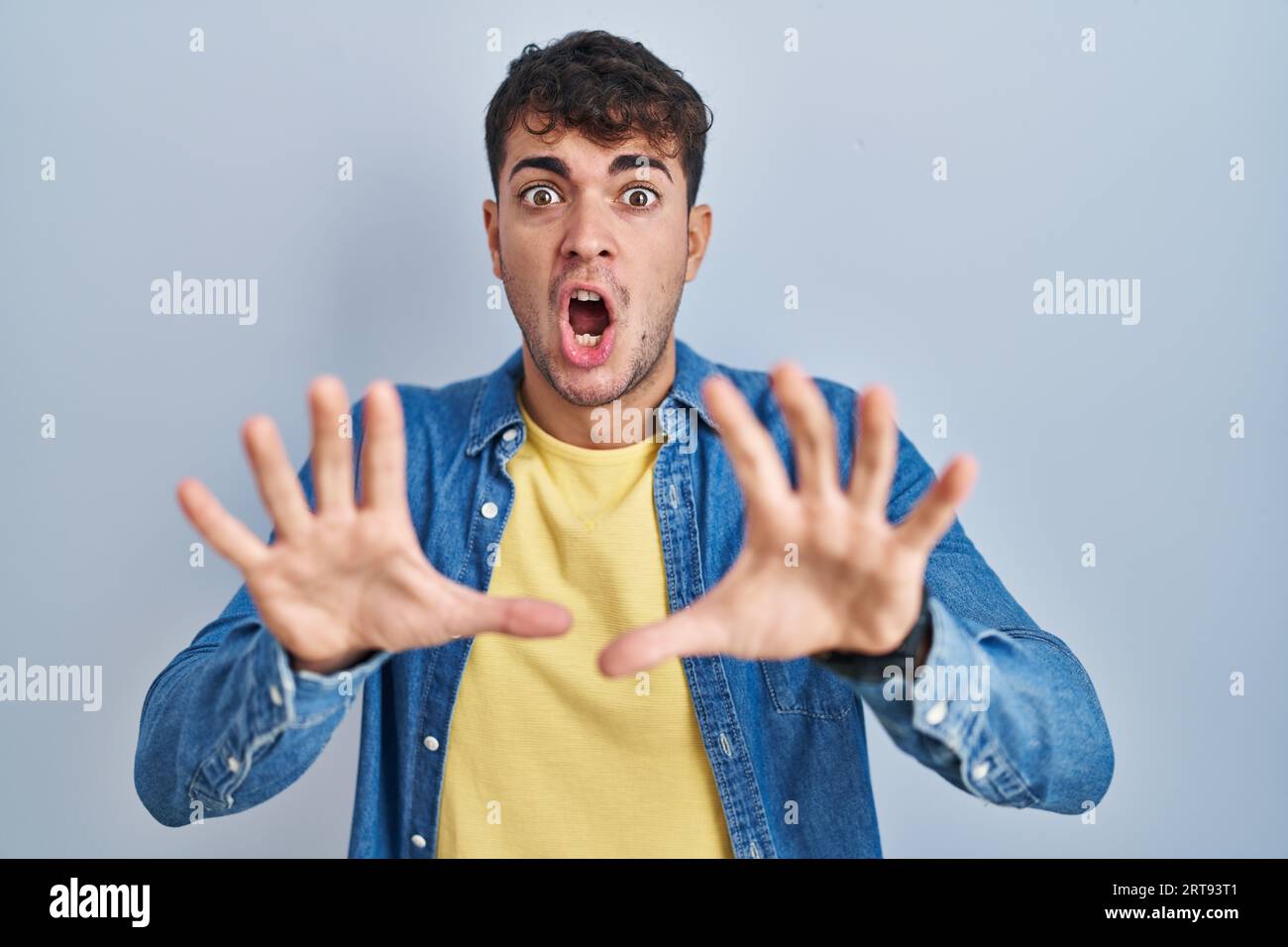 Young hispanic man standing over blue background afraid and terrified ...