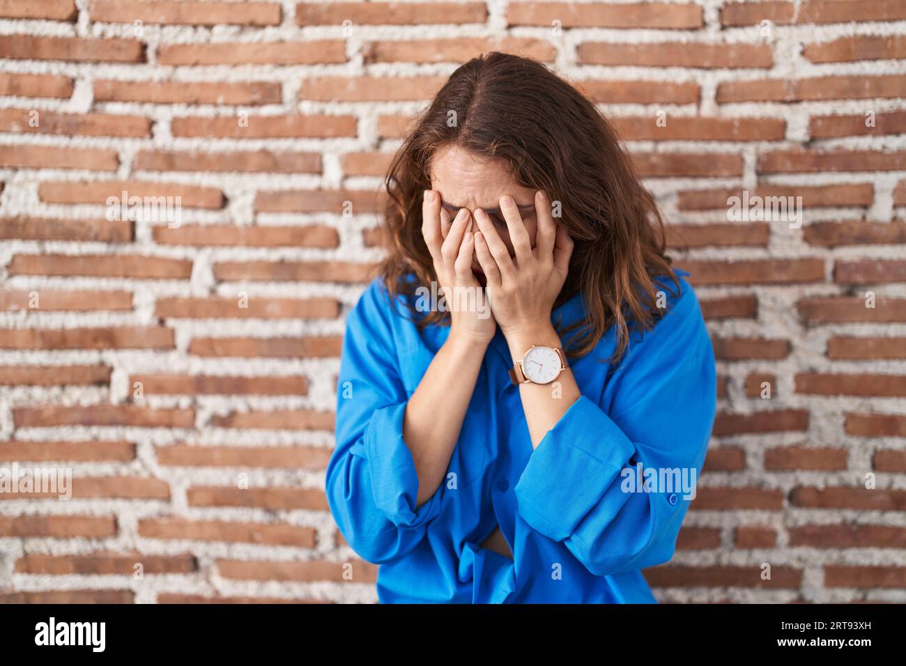 Beautiful brunette woman standing over bricks wall with sad expression ...