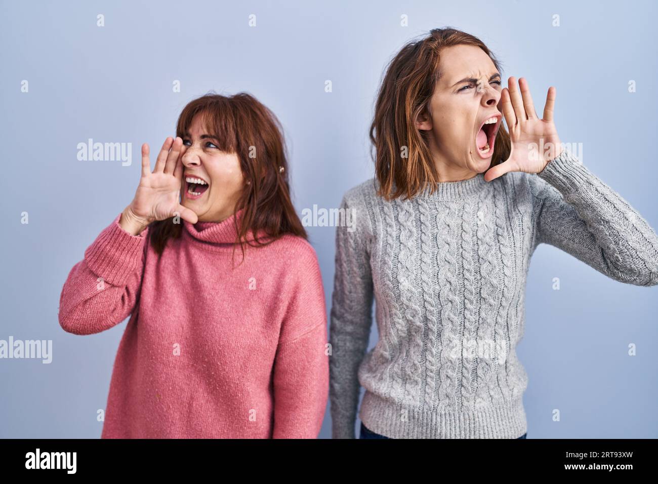 Mother and daughter standing over blue background shouting and ...